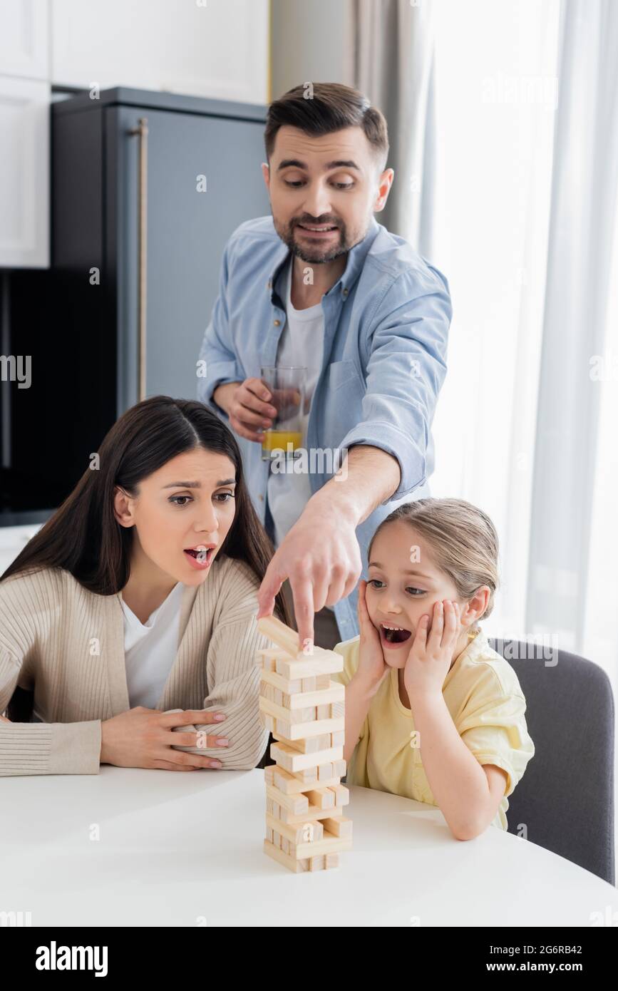 man with orange juice putting block on wooden tower near astonished ...