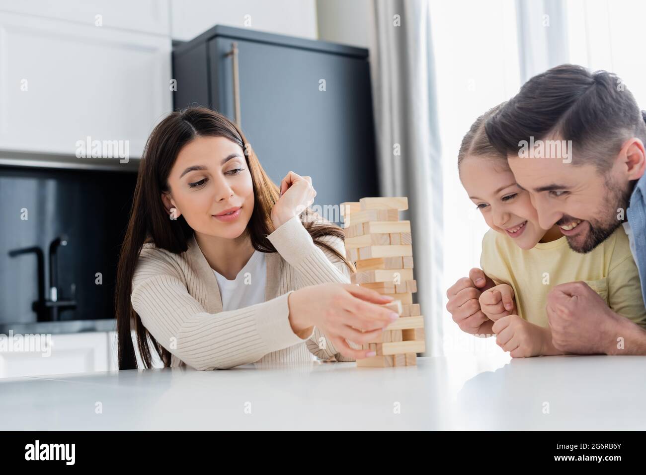 woman removing block from wooden tower near excited husband with ...