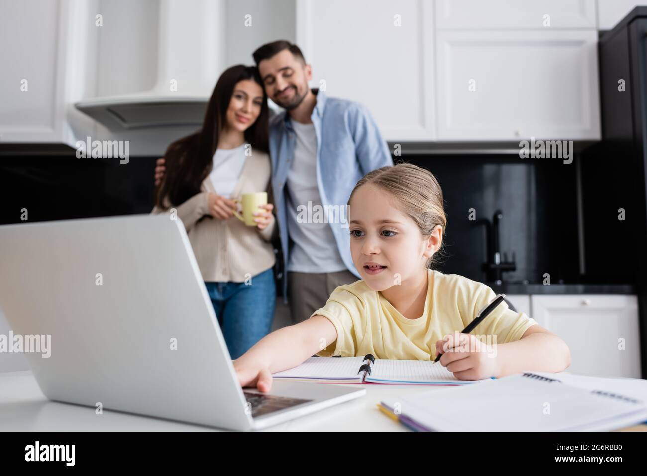 kid using laptop while doing homework near parents smiling on blurred ...
