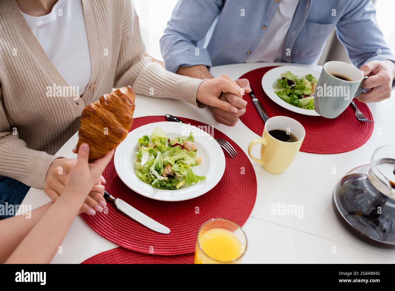 cropped view of girl holding croissant near parents and fresh vegetable ...