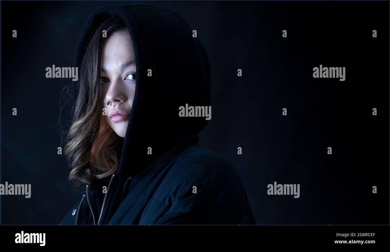 A young woman wearing her hood up, looking at the camera. The room is ...