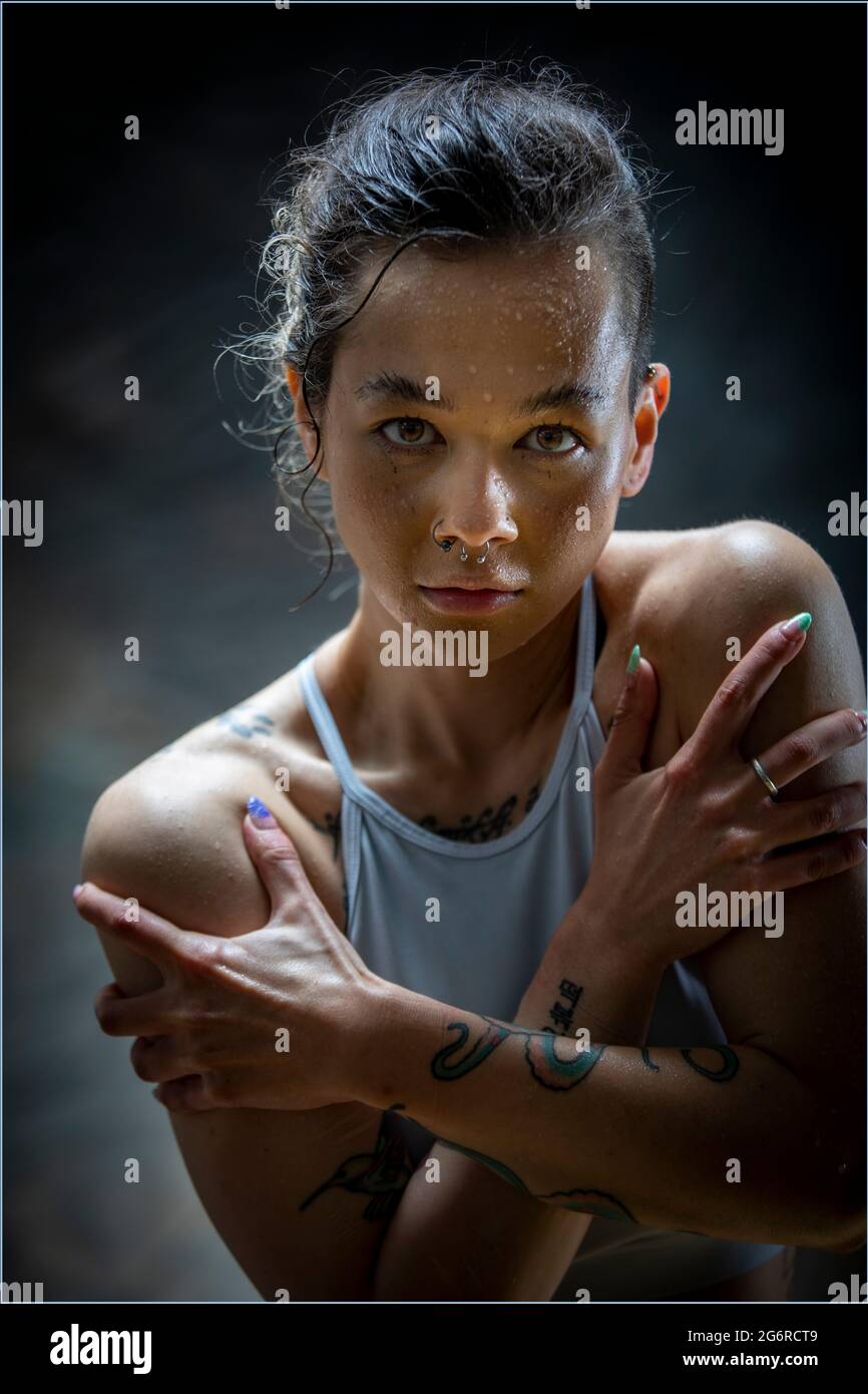A young woman with tattoos in sports clothing, she is embracing herself ...