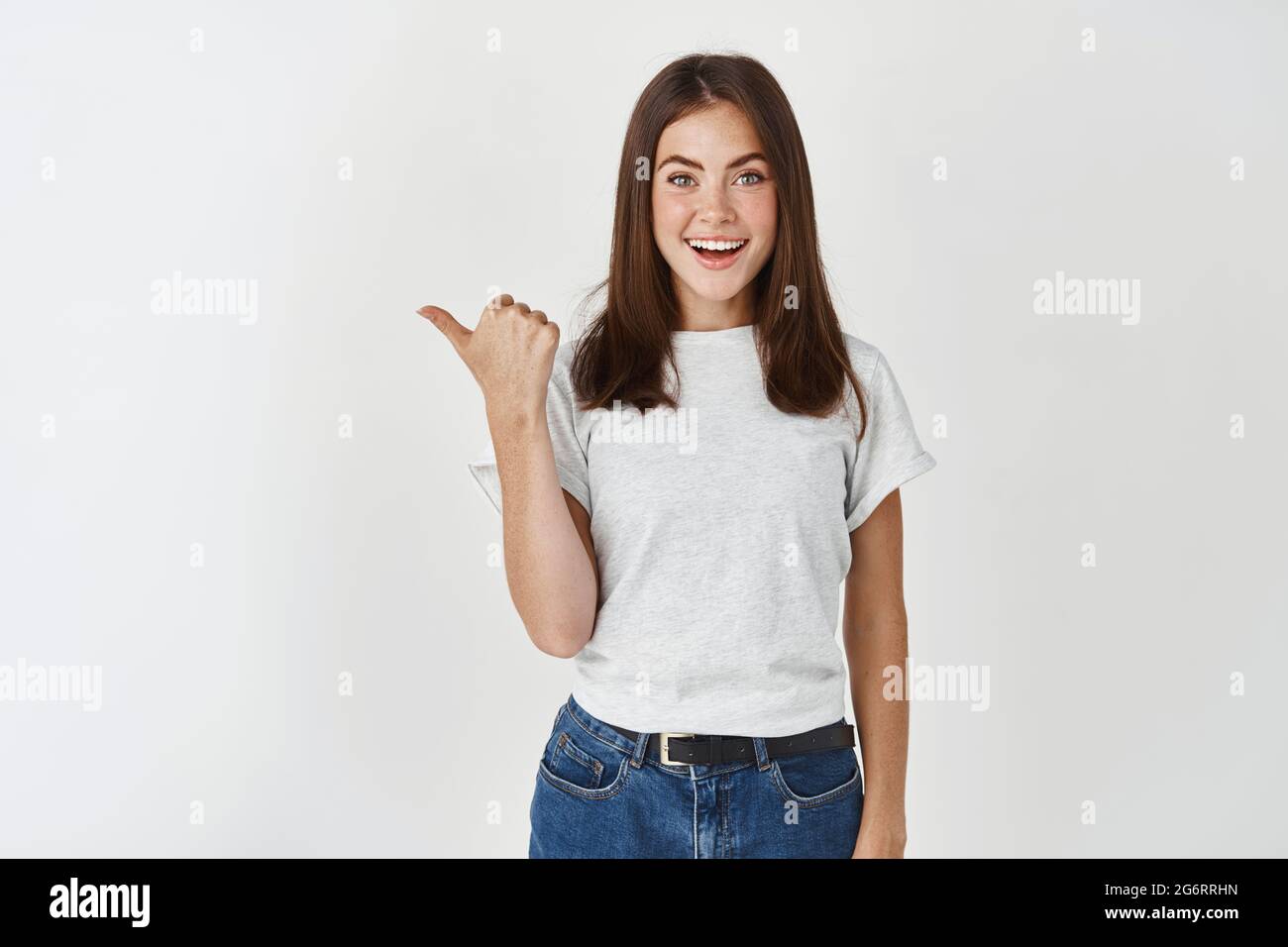Cheerful young woman pointing thumb left at copy space, showing promo ...
