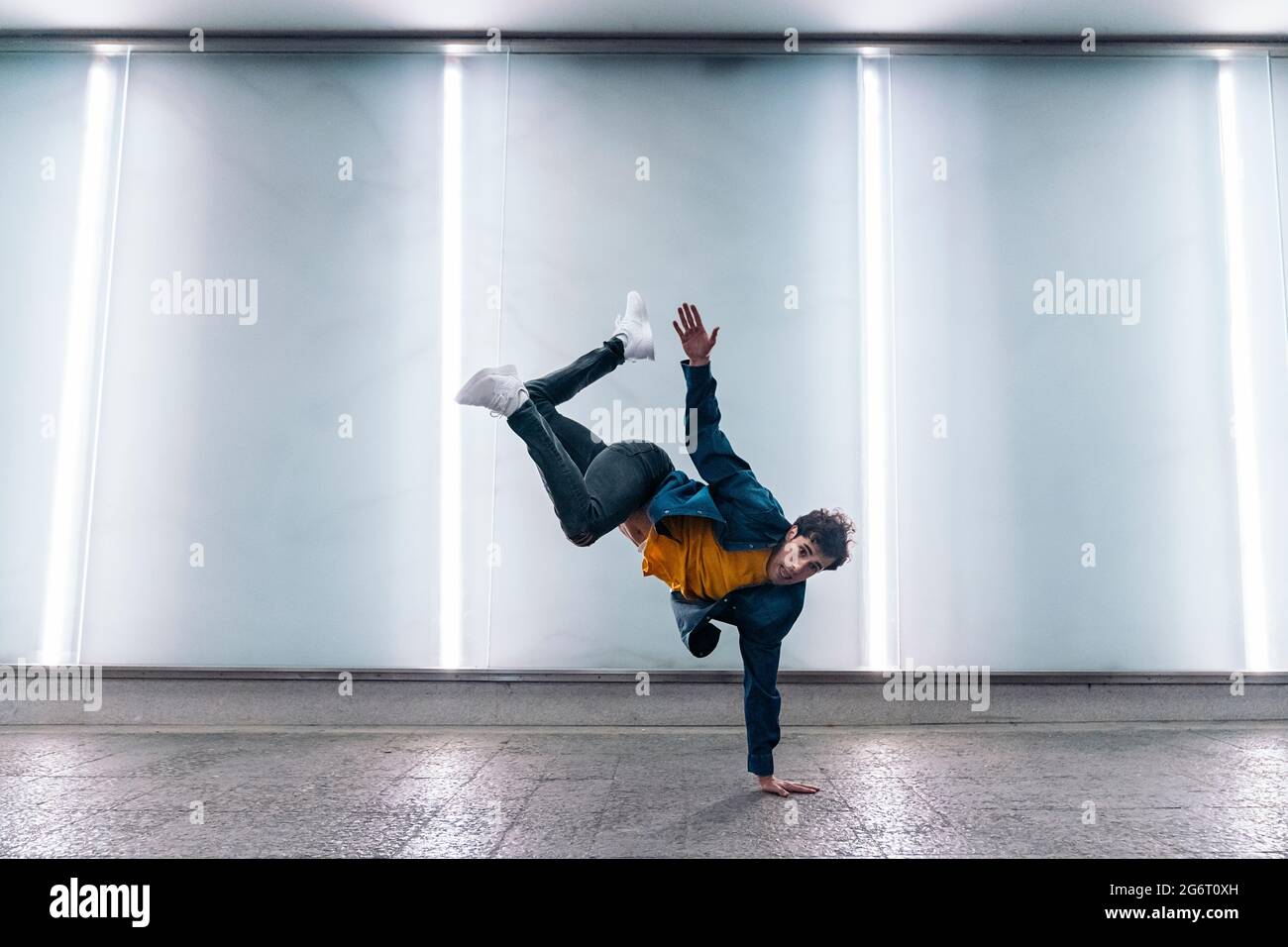 Talented young man dancing against white wall with lights and ...