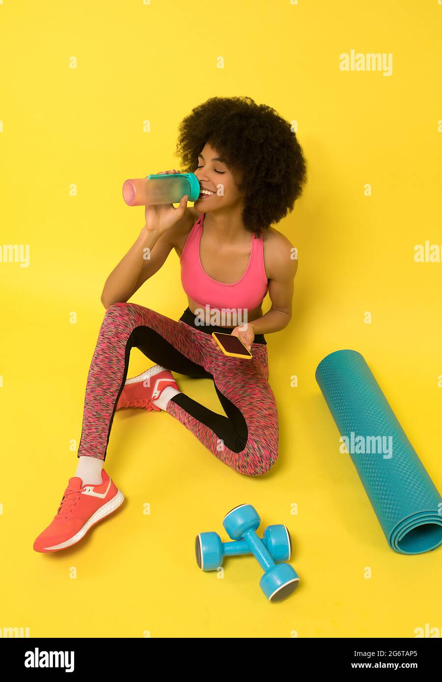 A young pretty curly-haired mulatta drinking water after a workout ...