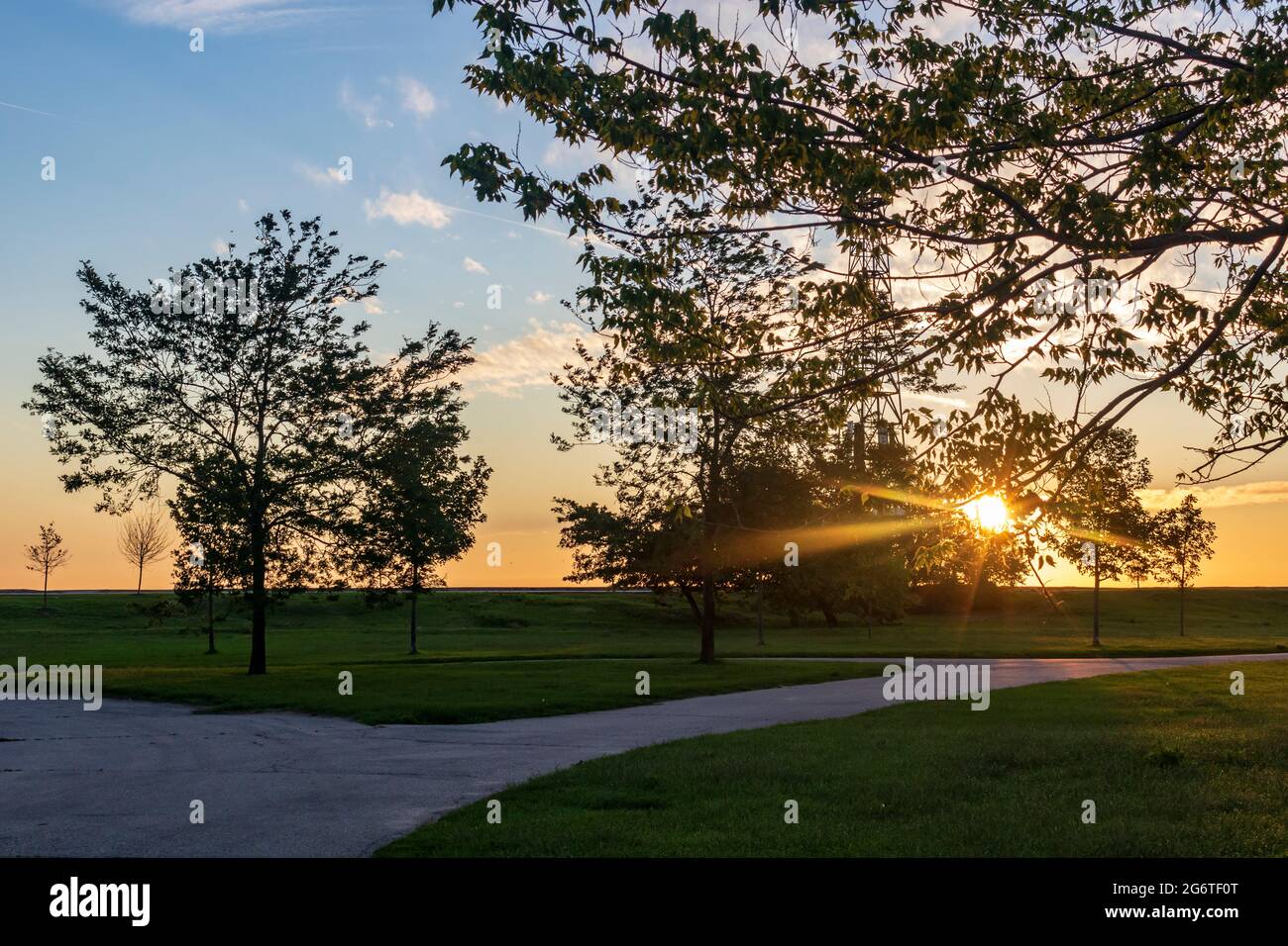 Sunrise peaking through trees along a path Stock Photo - Alamy
