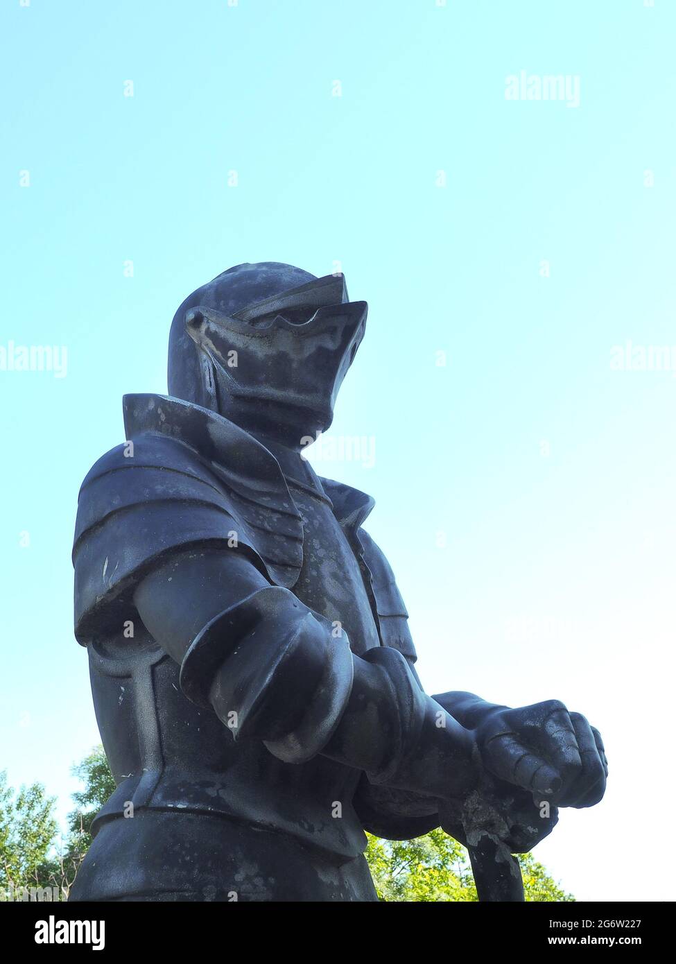 A stone monument of medieval knight in armor stands outdoors against a ...