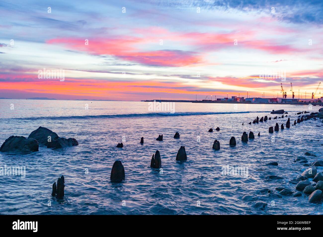 Coastal waterfront old pier posts leading to distant port facility and ...