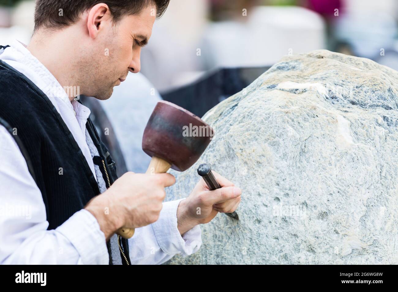 Sculptor with mallet and cutter working on erratic block Stock Photo ...