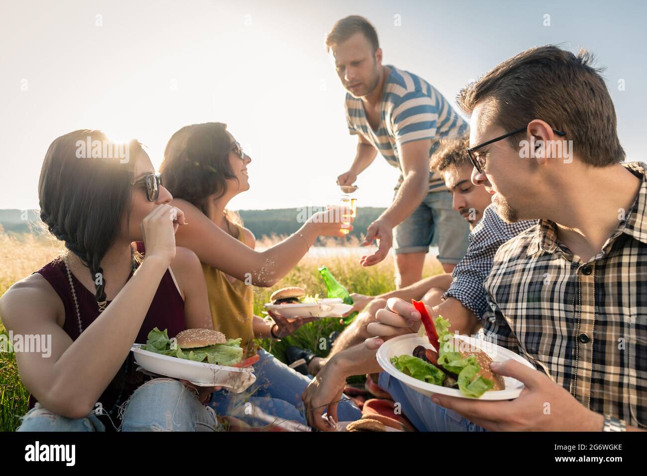 Young people having summer barbecue picnic and eating together sitting ...