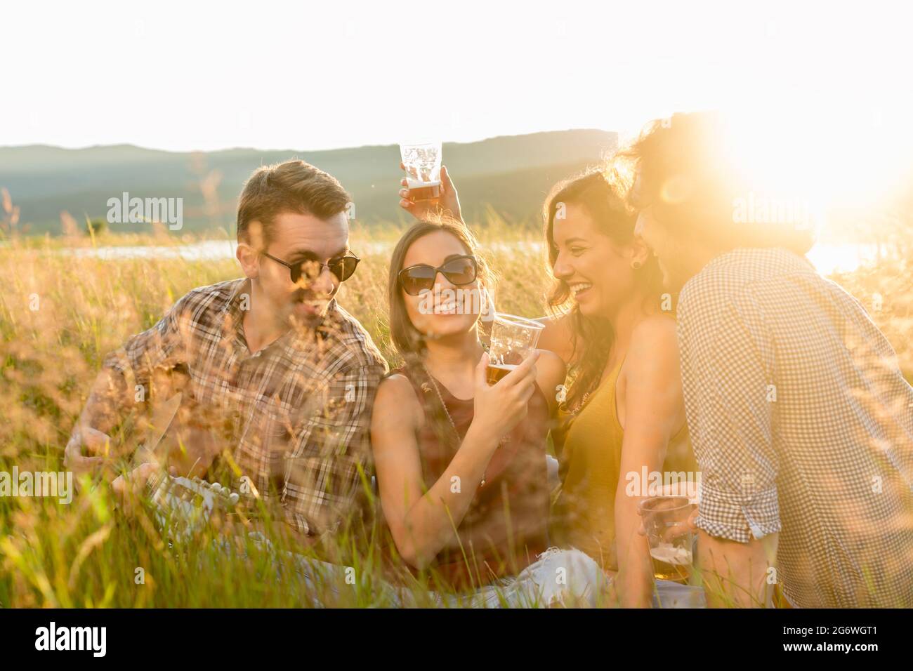 Friends enjoying evening mood of summer day sitting in high grass with ...