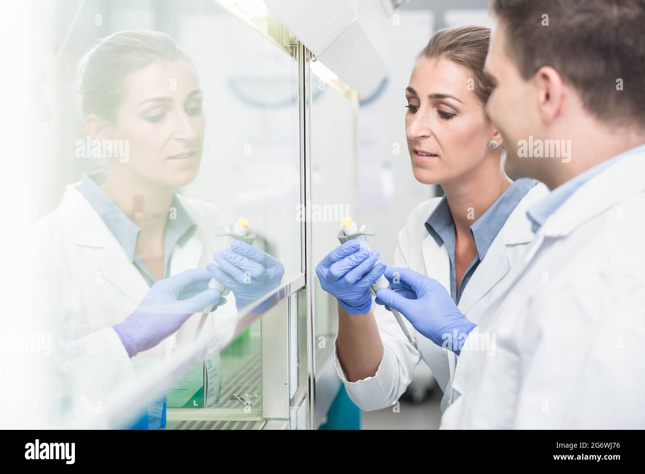 Scientists in laboratory preparing samples under splashback for ...