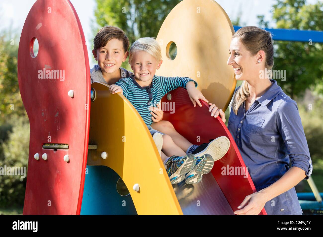 Happy family playing on adventure playground, children chuting chute ...