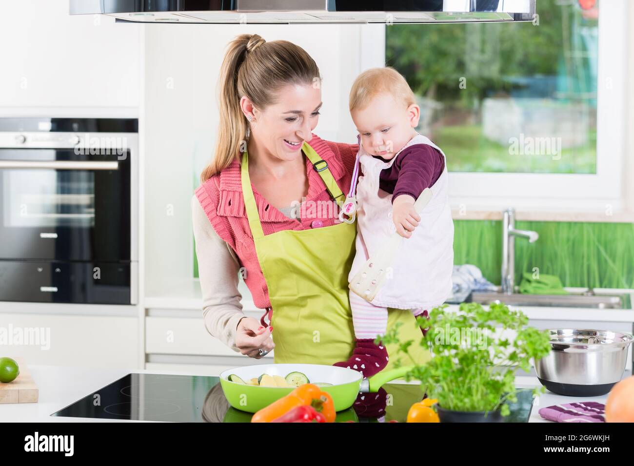 Mum cooking food with baby in arm Stock Photo - Alamy