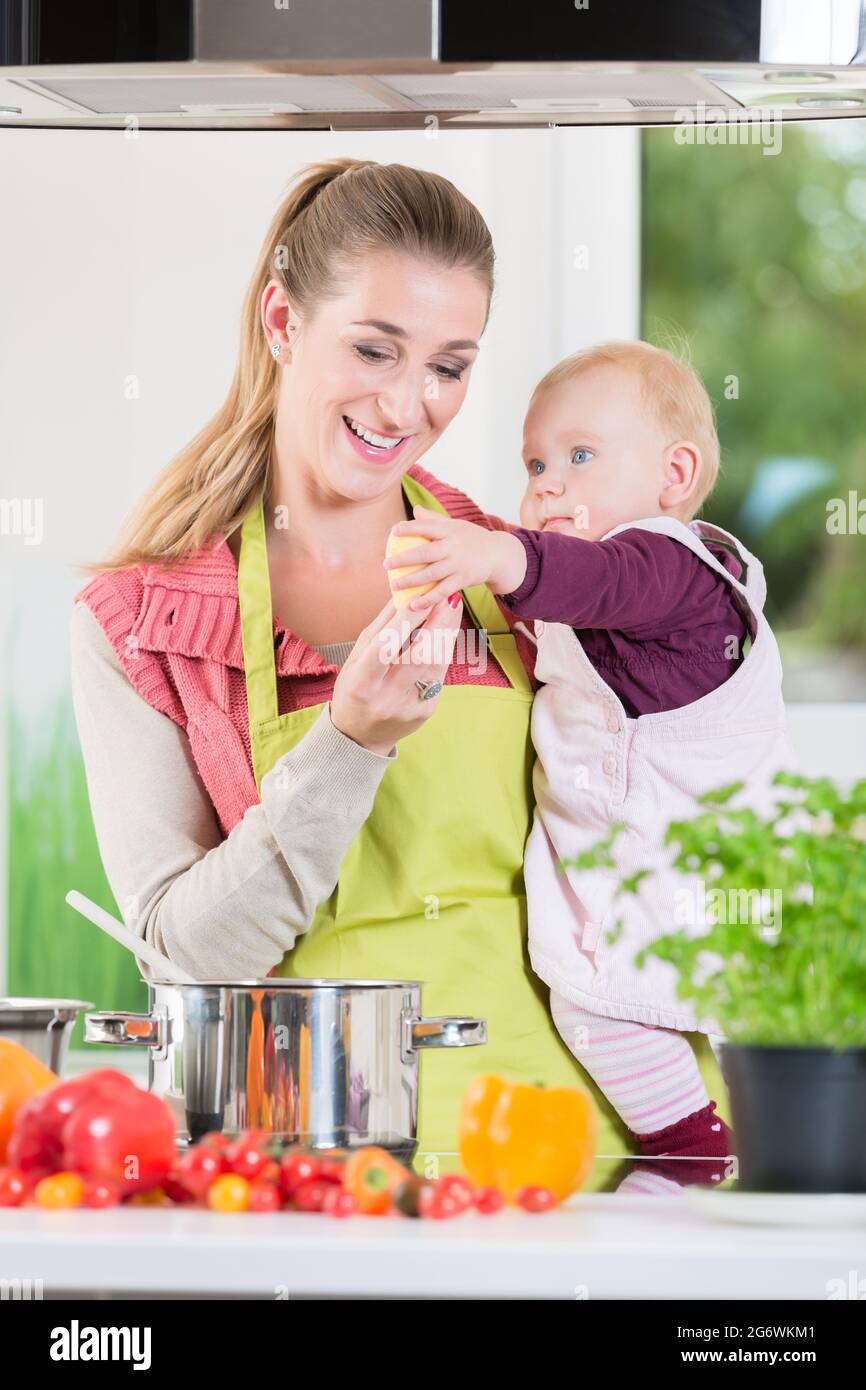 Happy mother working in kitchen while carrying child Stock Photo - Alamy