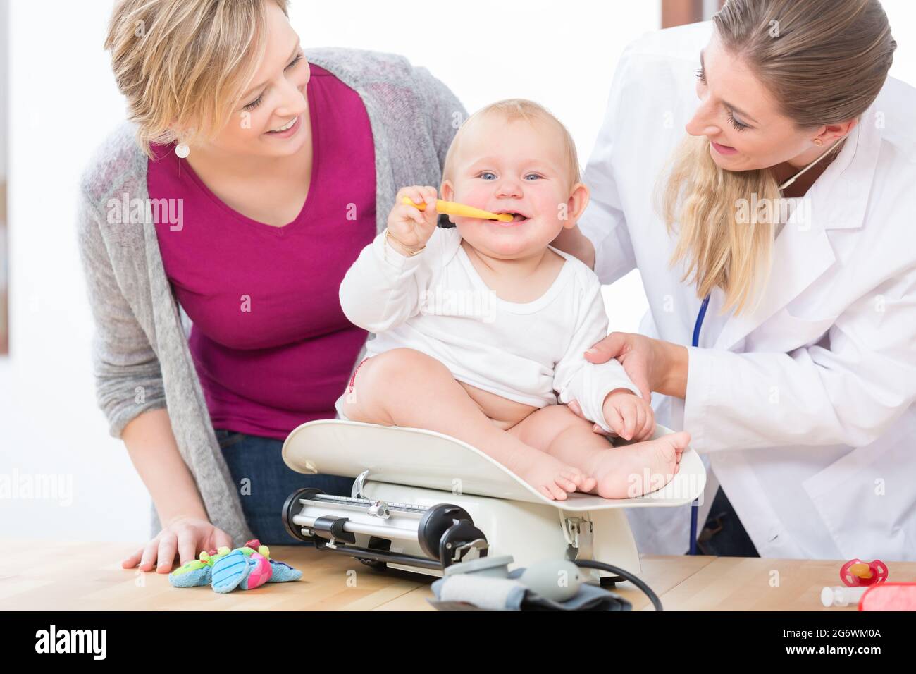 Female pediatric care specialist smiling while measuring the weight of ...