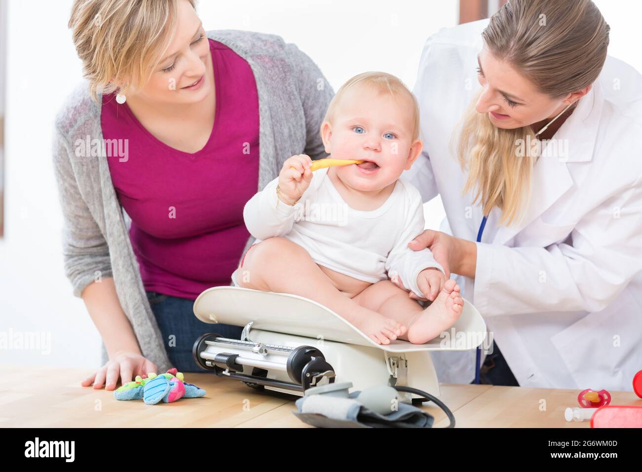 Female pediatric care specialist smiling while measuring the weight of ...