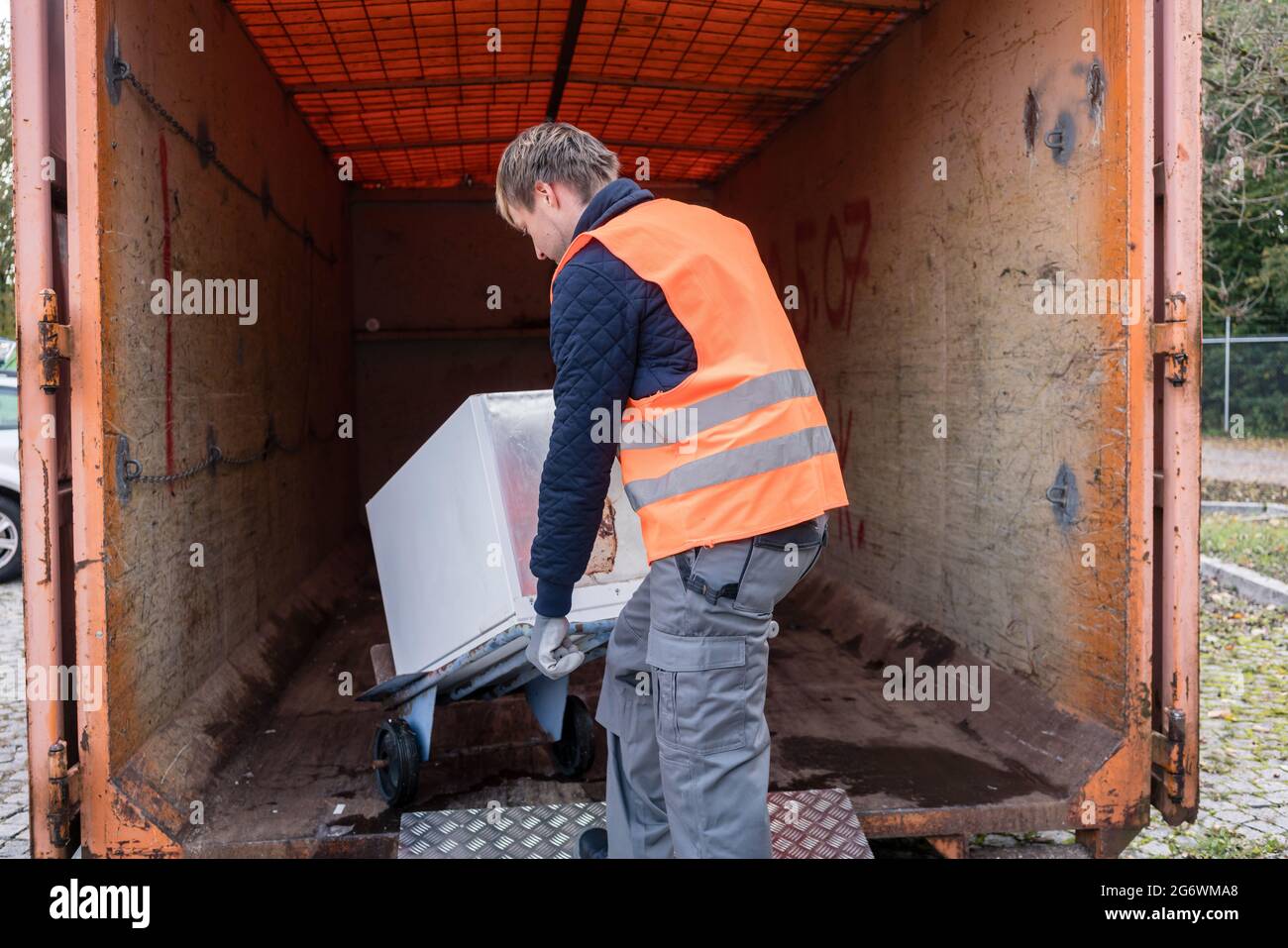 Worker putting old washing machine in container Stock Photo - Alamy