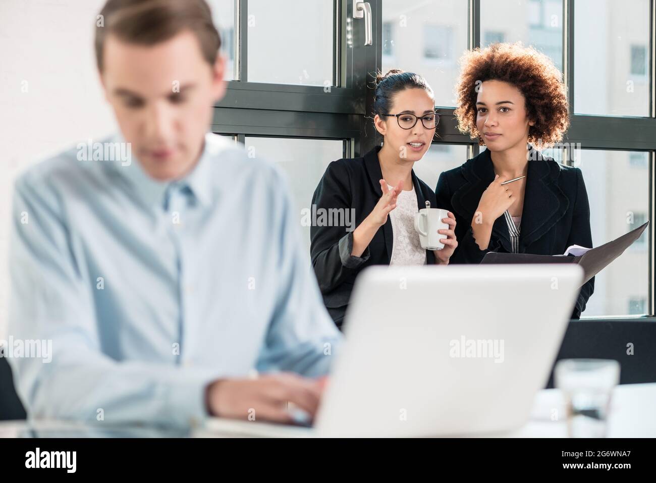 Two young cheerful female employees talking in the office next to their ...
