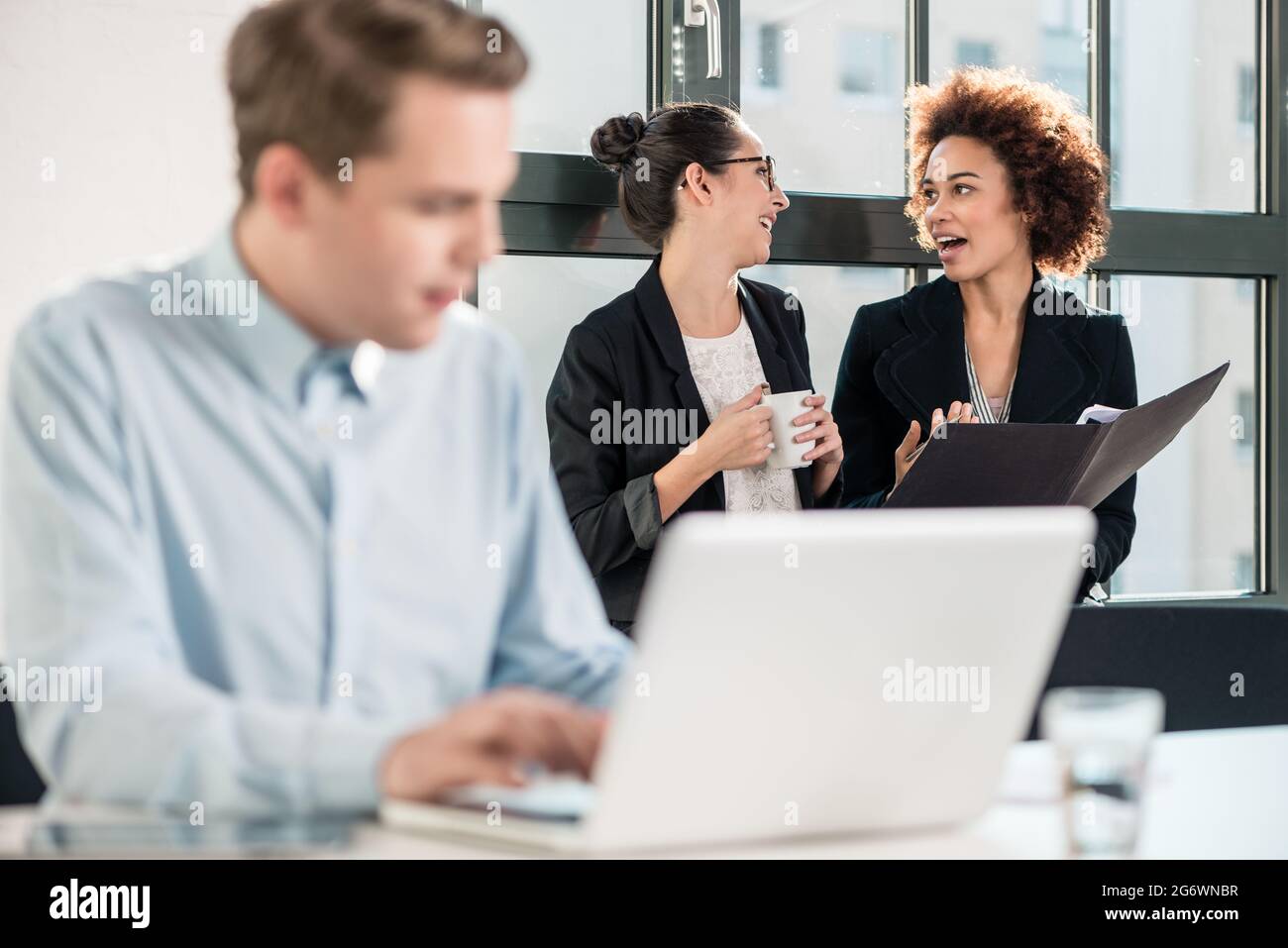 Two young cheerful female employees talking in the office next to their ...