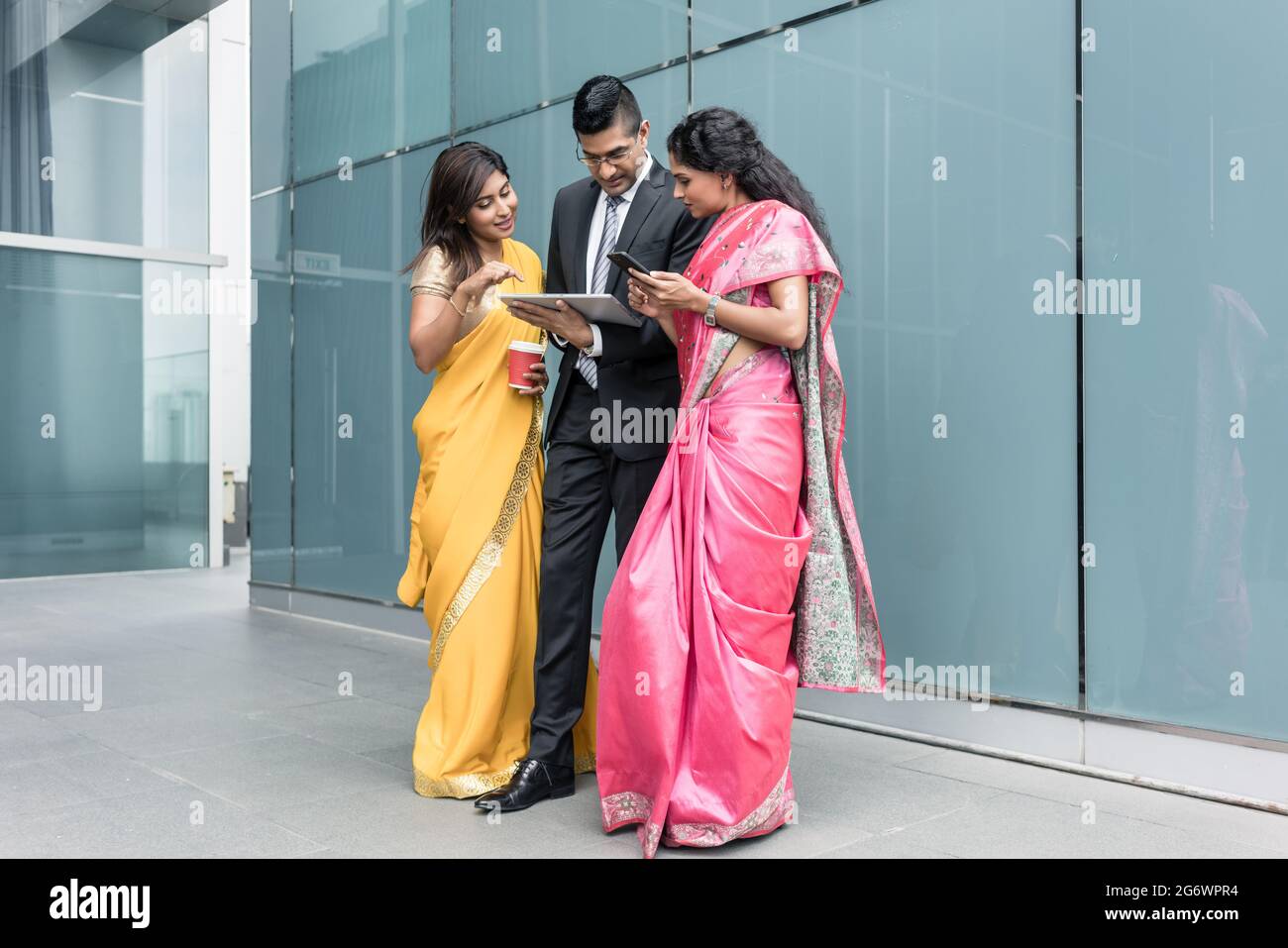 Three Indian business people using high-tech devices outdoors during ...