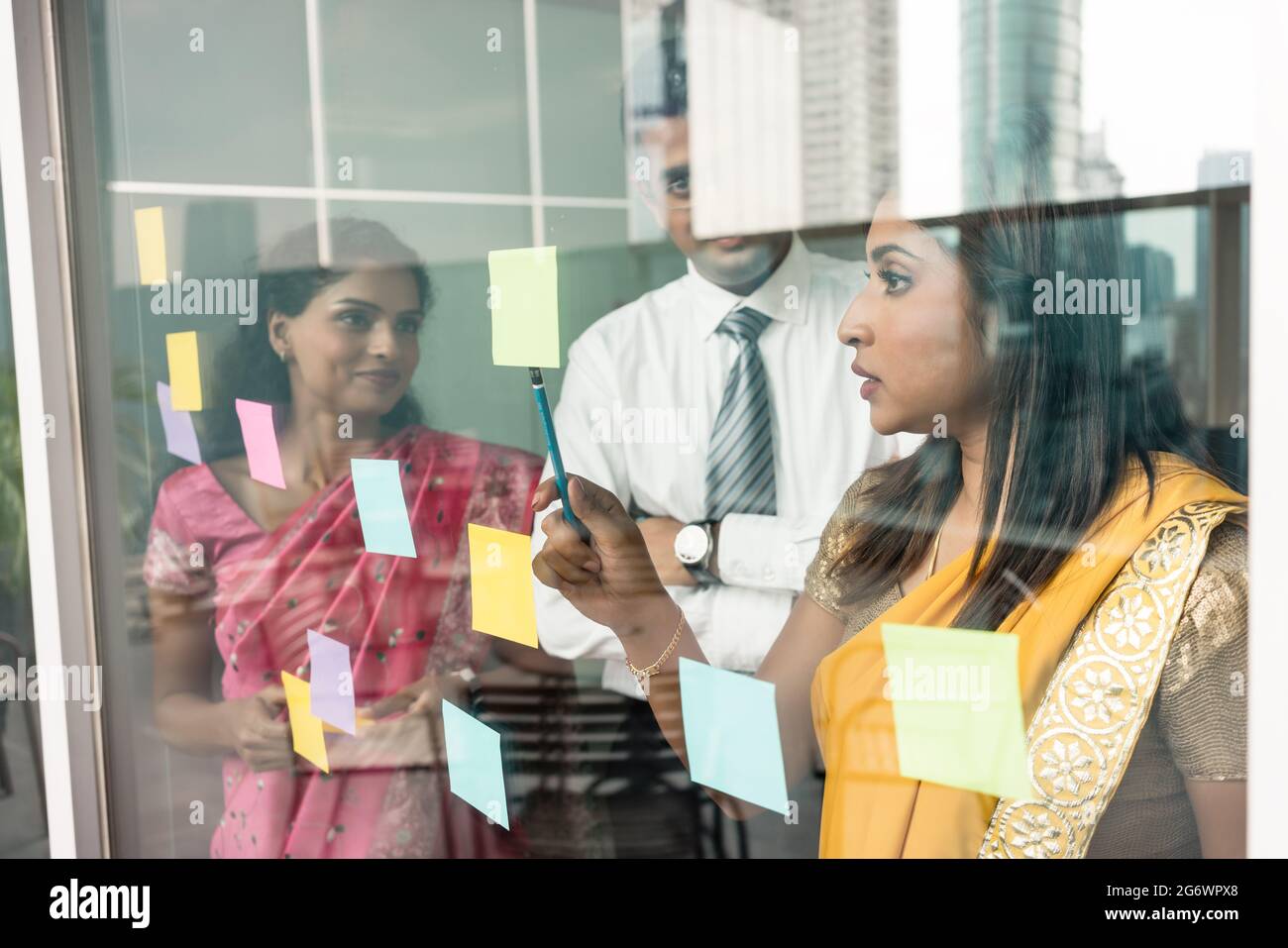Three Indian employees sticking reminders on glass wall with business ...