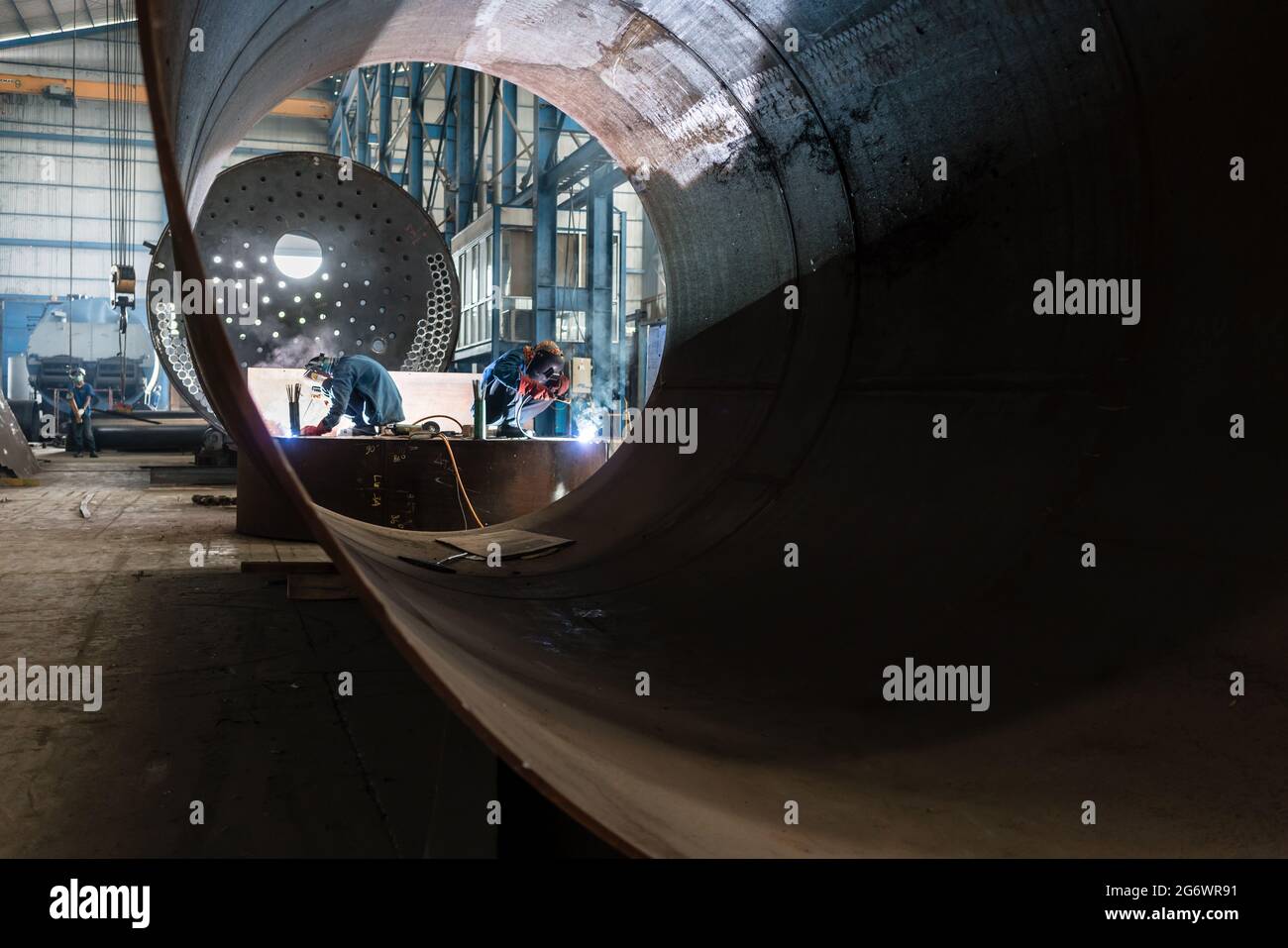 Two workers welding in the interior of a factory manufacturing metallic ...