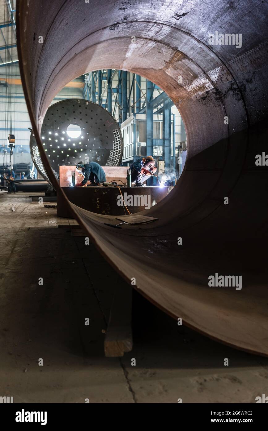 Two workers welding in the interior of a factory manufacturing metallic ...