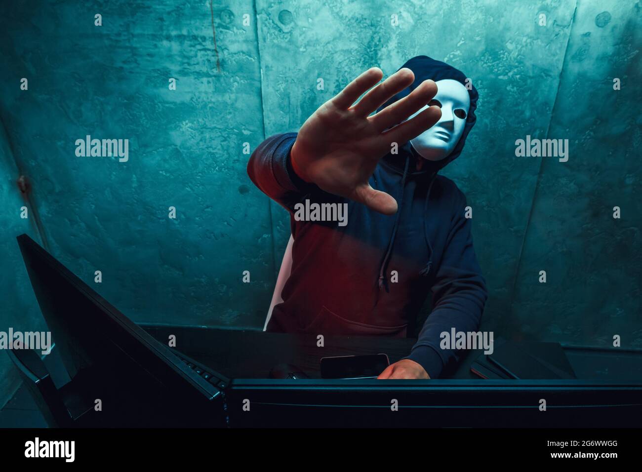 Anonymous hacker wearing face mask working on computer in dark room ...