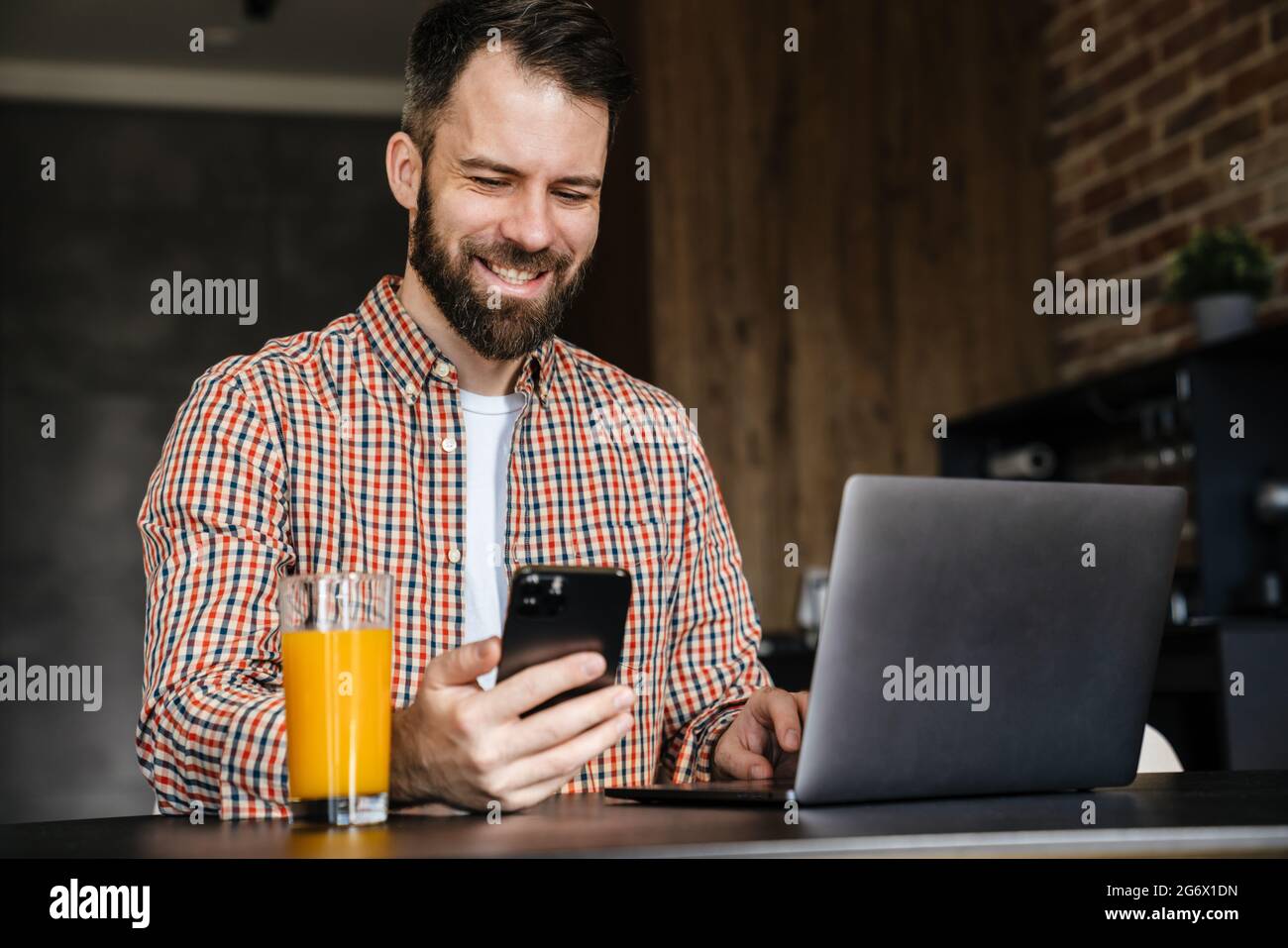 Happy mid aged brunette bearded man sitting at the table looking at ...