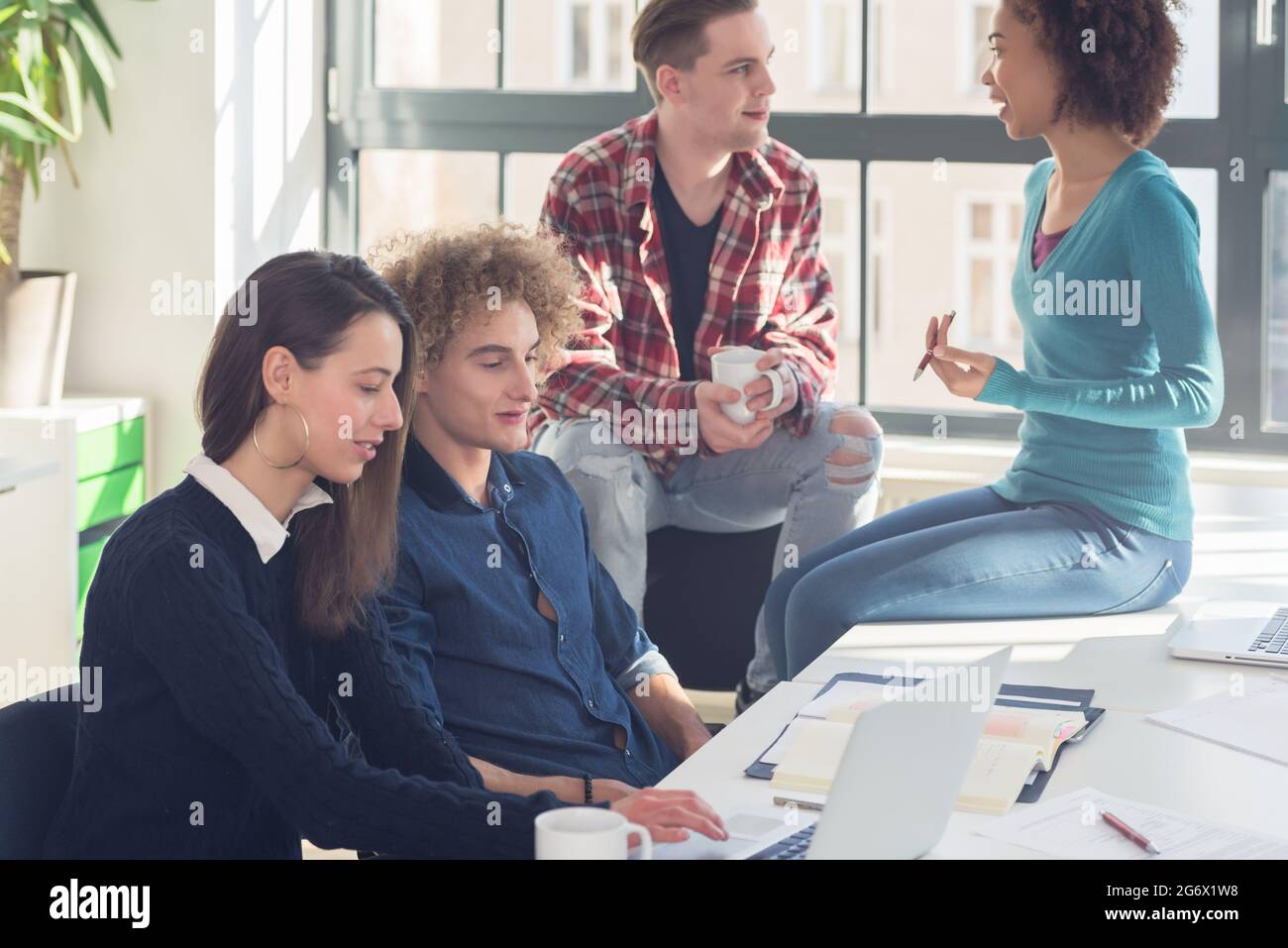 Four young students watching together a funny online video on a laptop ...