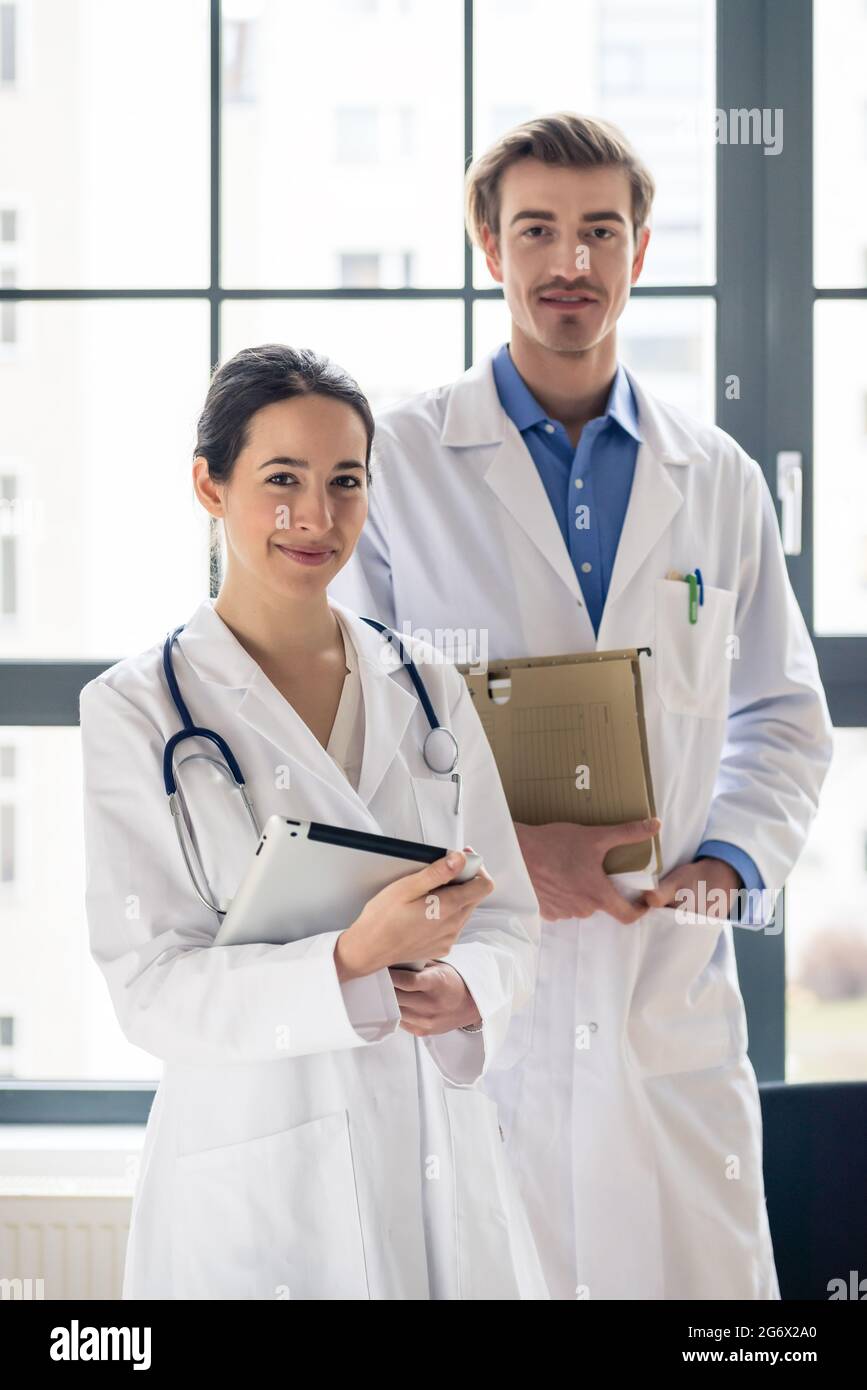 Portrait of two determined physicians wearing white medical gowns while ...