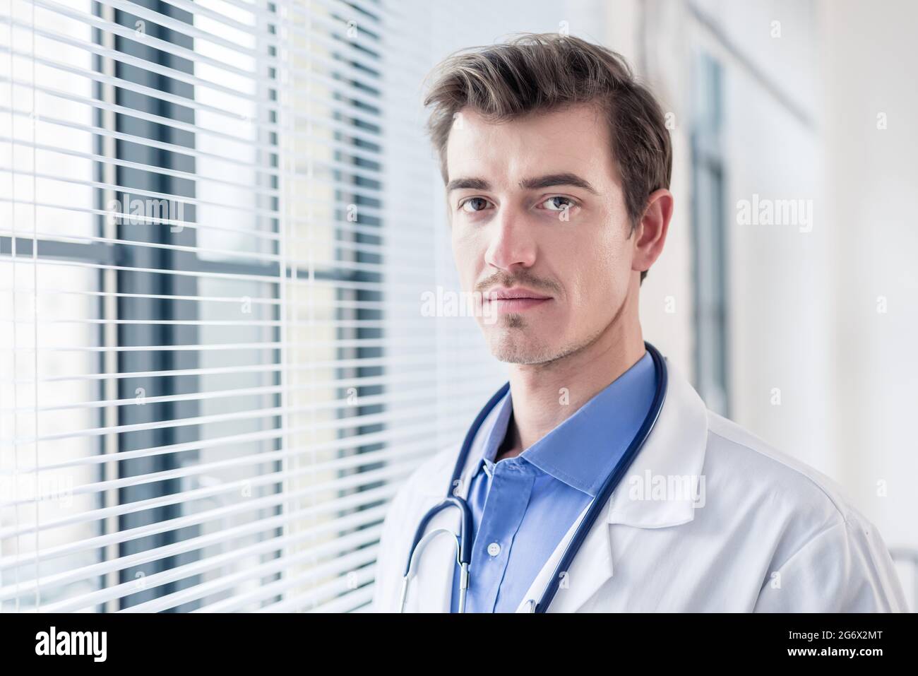 Close-up portrait of a young serious doctor looking at camera with ...