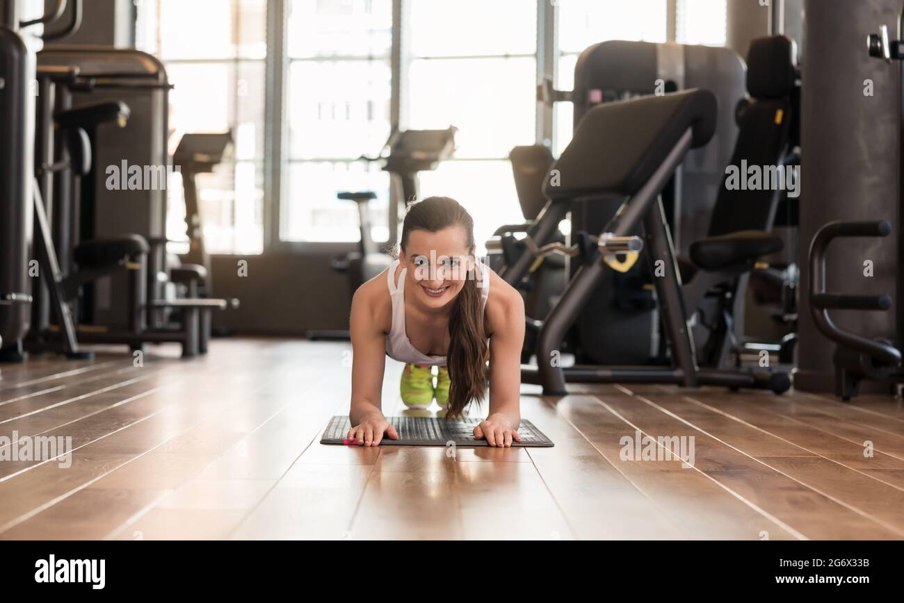 Front view of a young fit woman smiling while practicing the forearm ...
