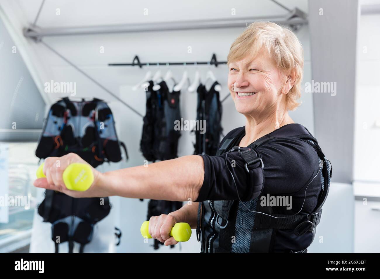 Fit Senior lady staying fit with dumbbell exercise in wireless ems gym ...