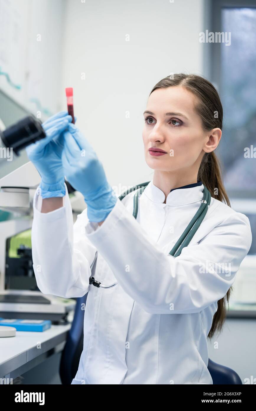 Doctor in medical laboratory looking at blood test she is holding in ...