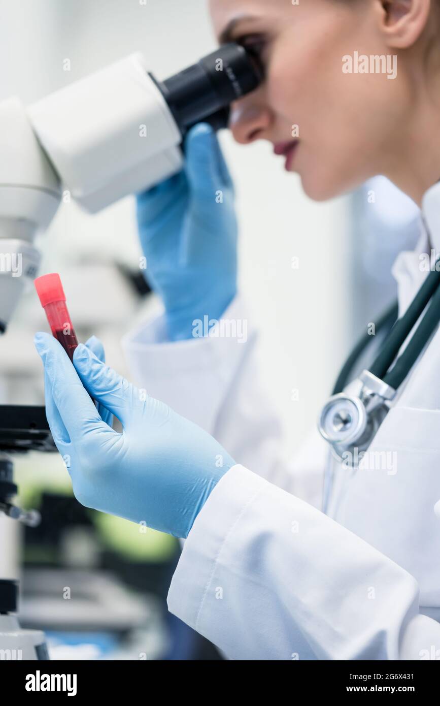 Woman examining blood sample under microscope in medical or scientific ...