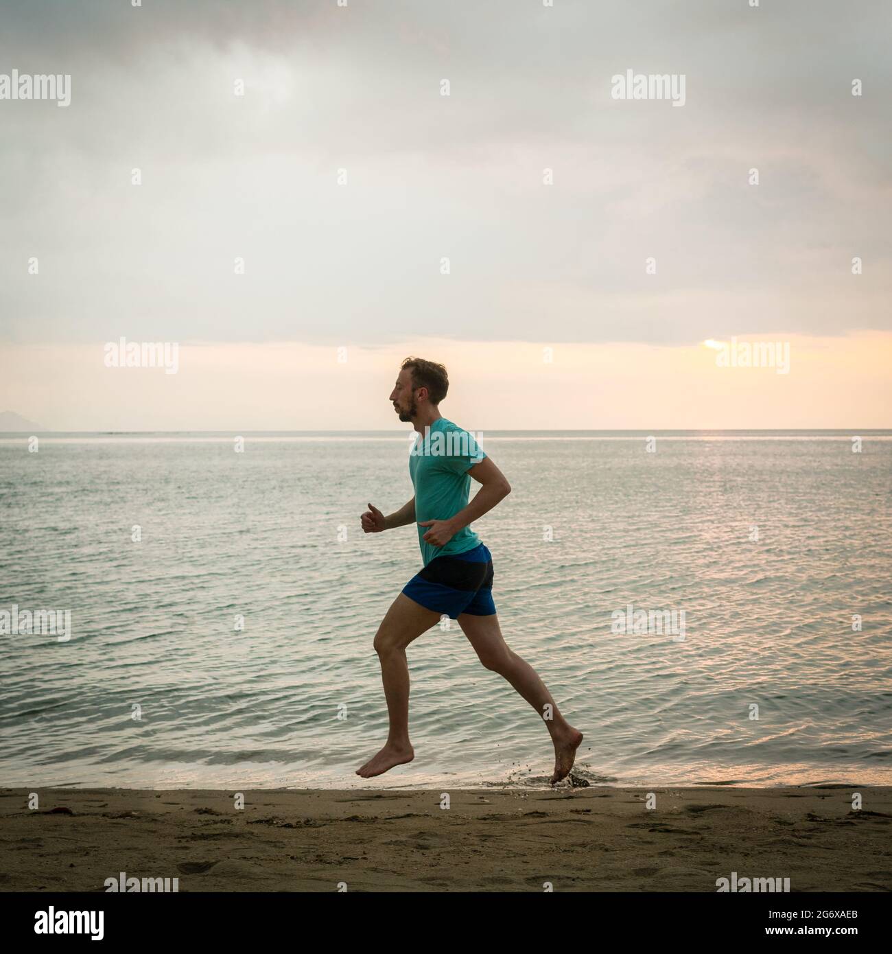 Full length side view of an athletic young man running on the beach ...
