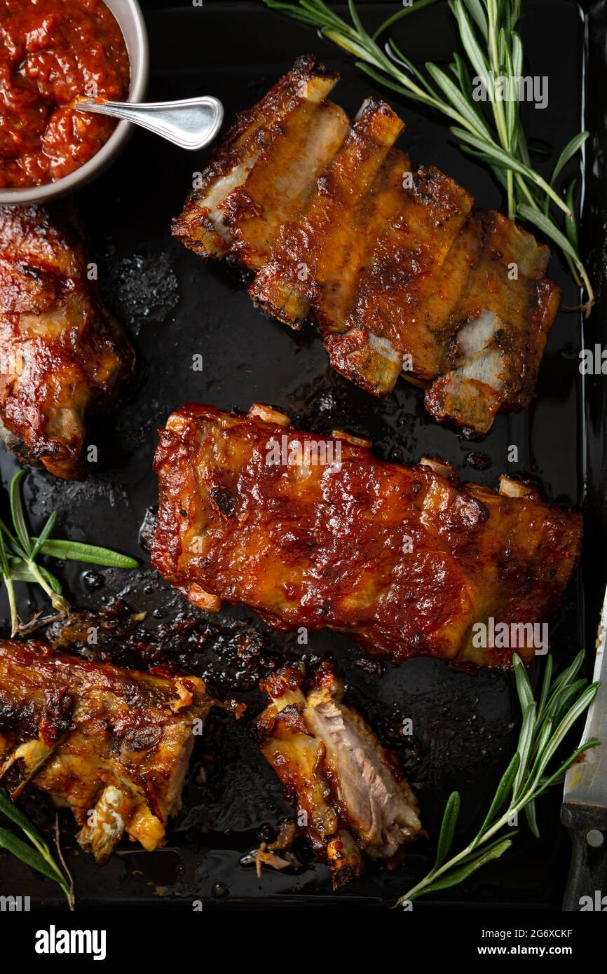 Overhead view of barbecue smoked ribs with red sauce on black surface ...