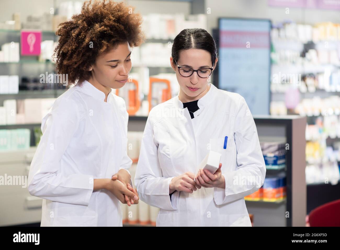 Two experienced female pharmacists wearing lab coats while analyzing ...