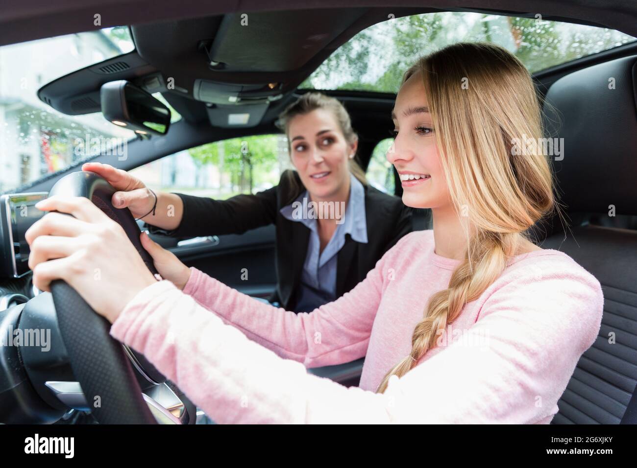 Student on wheel of car in driving lesson with her teacher learning to ...