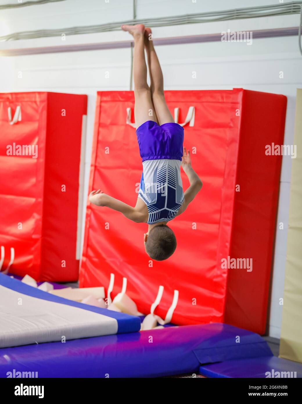 A young athlete performs a jump somersault in the gym. The athlete is ...