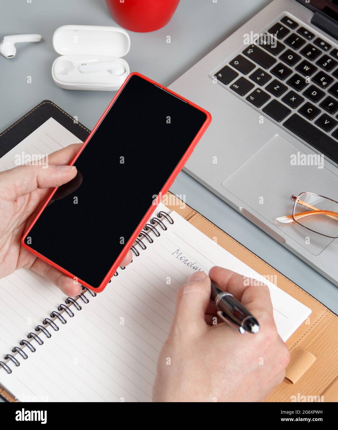 Man writing in agenda MONDAY and using cell phone on a grey office desk ...