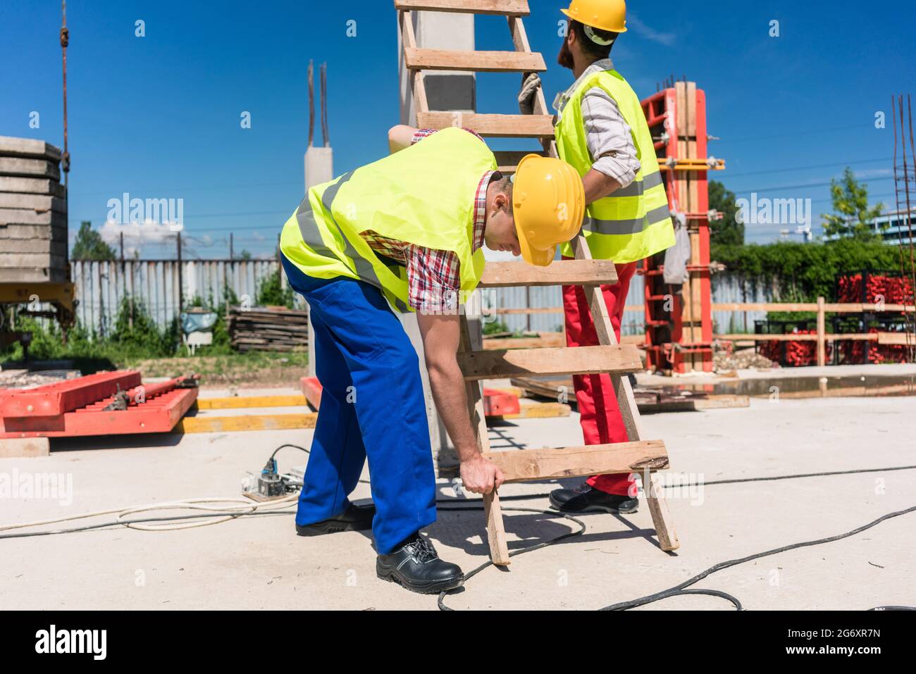 Two young blue-collar workers leaning a wooden ladder on the pylon of ...