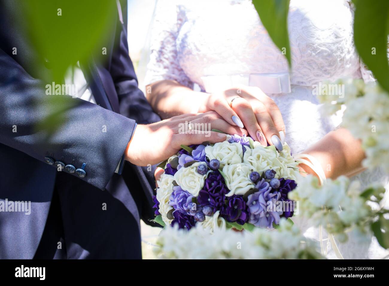 Hands of bride and groom close up with golden rings and bridal bouquet ...