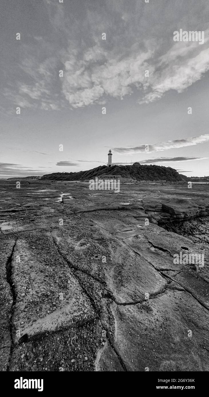 Vertical grayscale shot of a landscape with a lighthouse in the ...