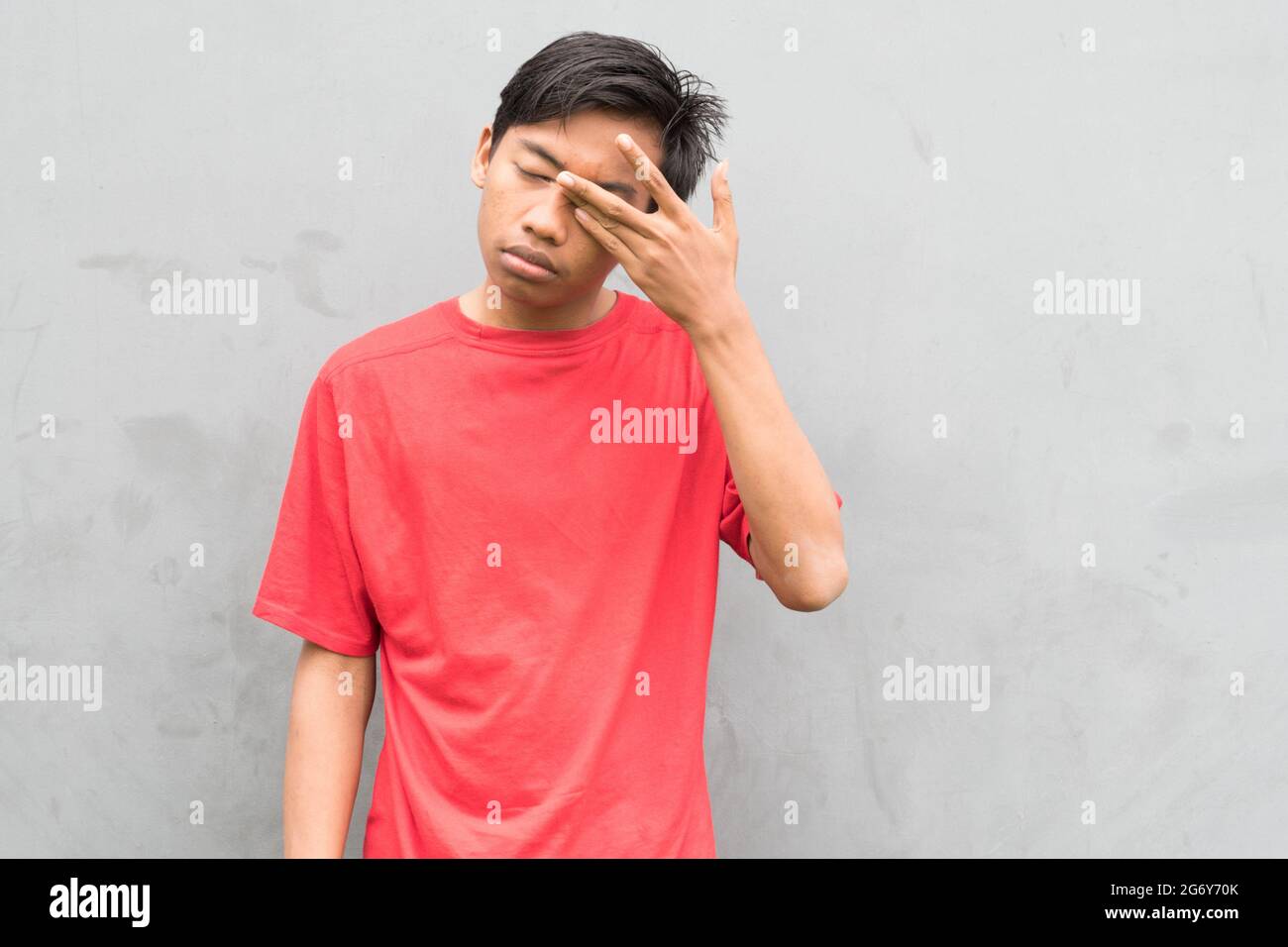 Young Indonesian guy wiping his eye after waking up on a gray wall ...