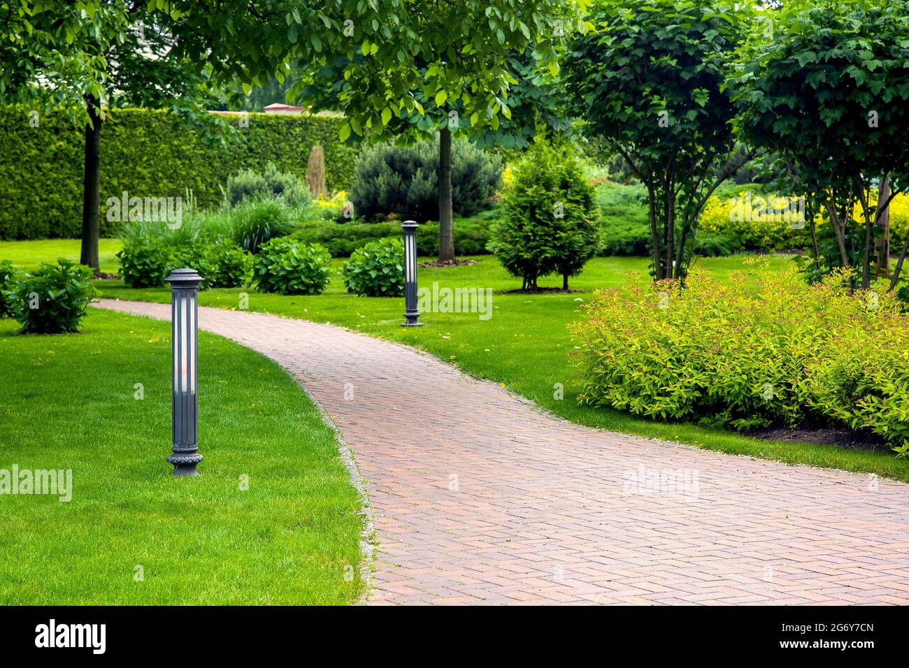 curved pedestrian pavement of stone tiles in park with landscaping and ...
