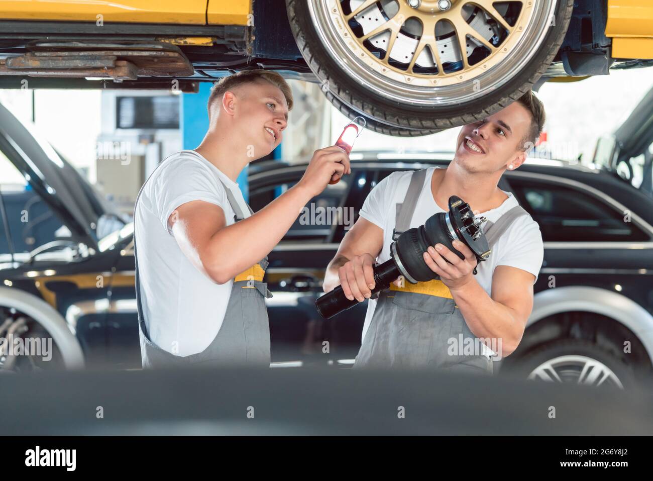 Two skilled auto mechanics analyzing together the rims of a lifted car ...