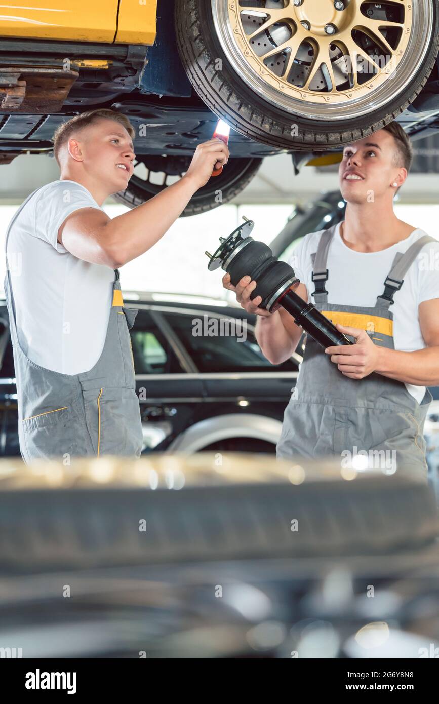 Two skilled auto mechanics analyzing together the rims of a lifted car ...
